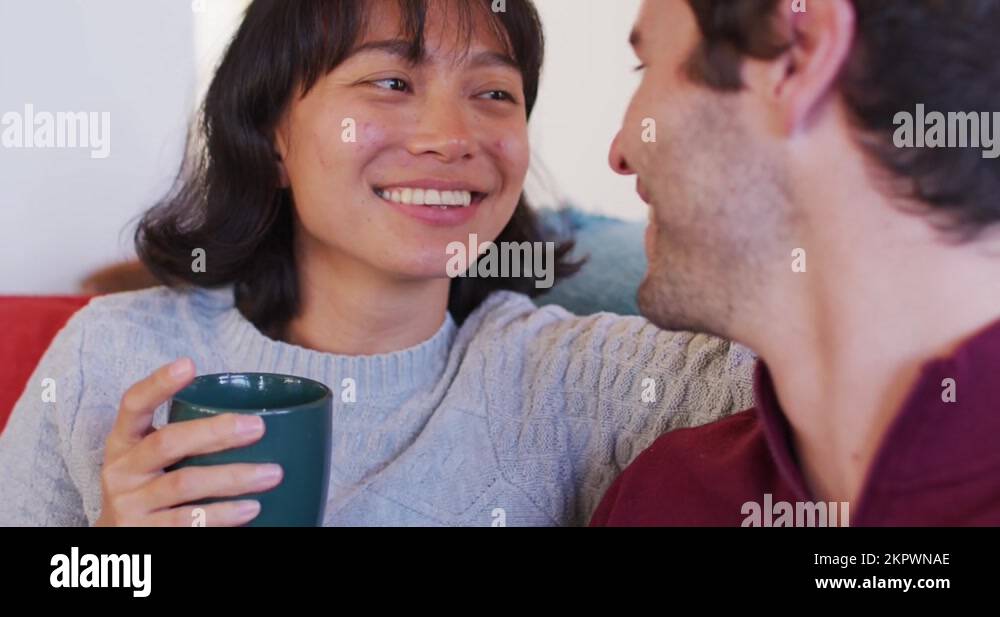 Video of back view of happy diverse couple sitting on sofa and drinking ...