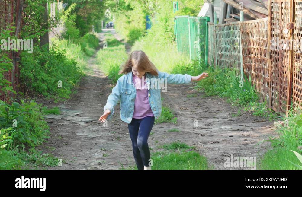 little girl have fun walking and running along the path in the village ...