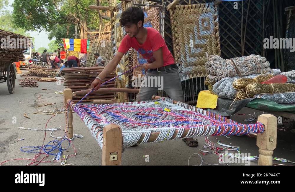 A worker ties rope to prepare a sustainable affordable wooden cot Stock ...
