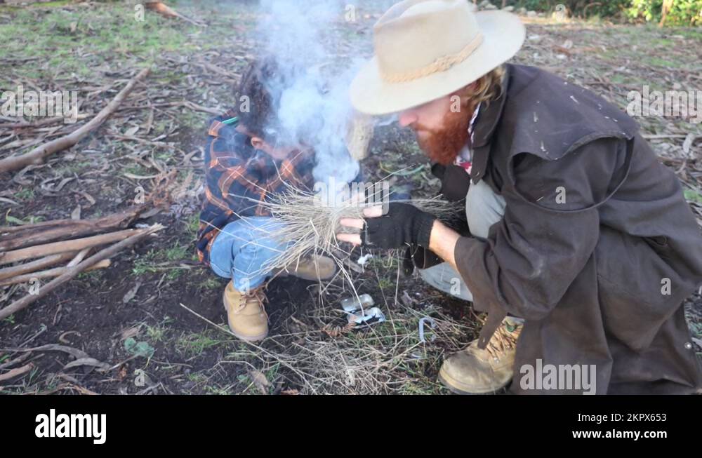 A bushman in a stockman jacket creates fire from a spark with his son ...