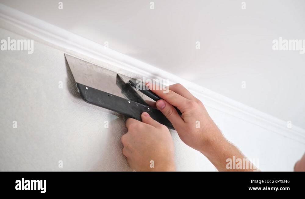 man cuts wallpaper near ceiling moldings using box cutter and putty ...