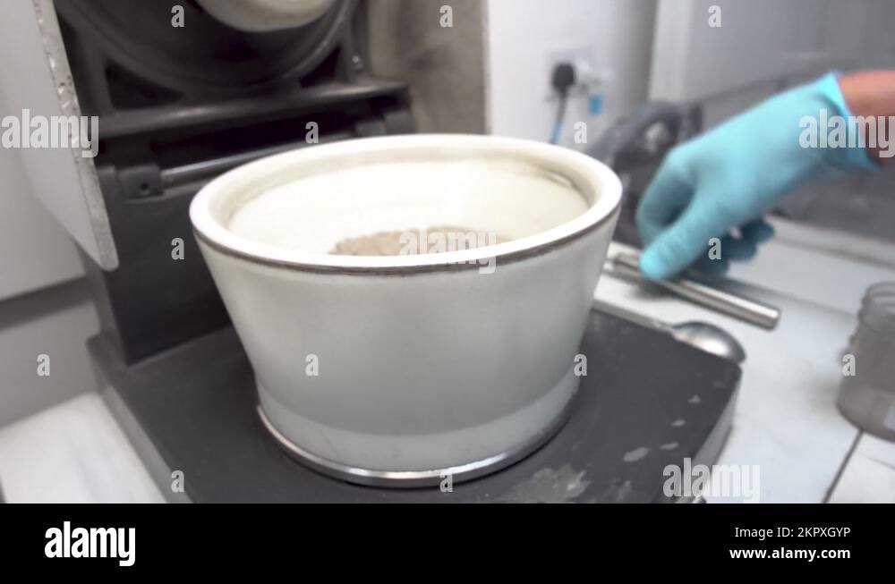 Lab worker opens and scoops powder from grinding mill into a container ...