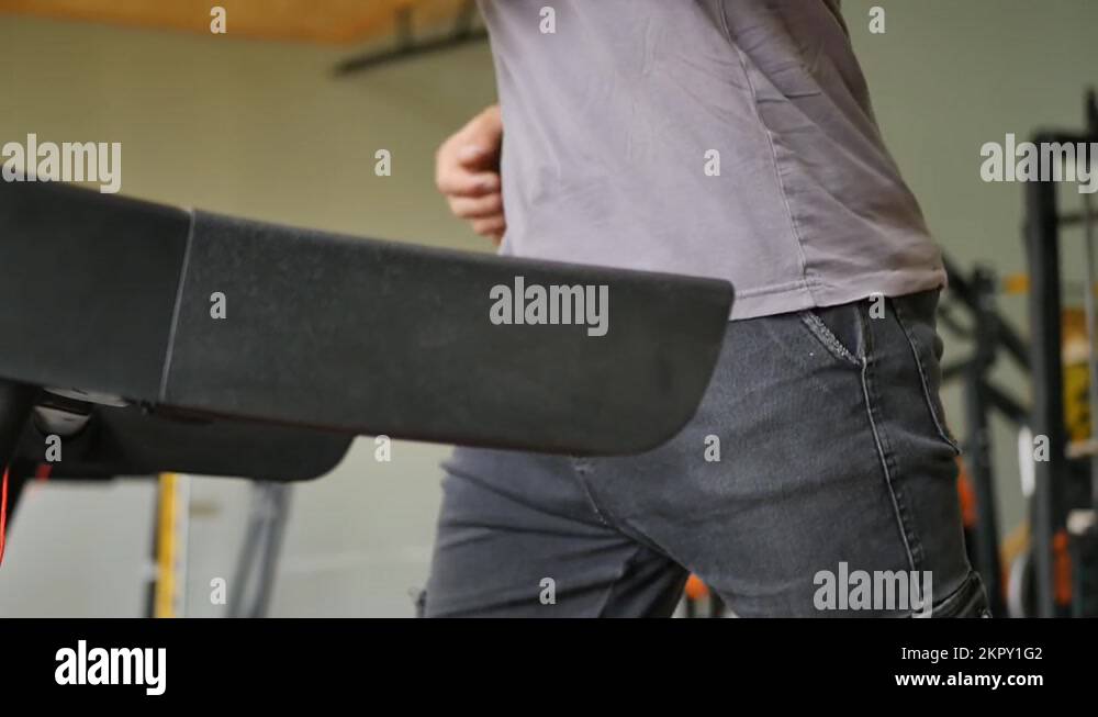 A young man runs on a treadmill accelerating to a medium pace in slow ...