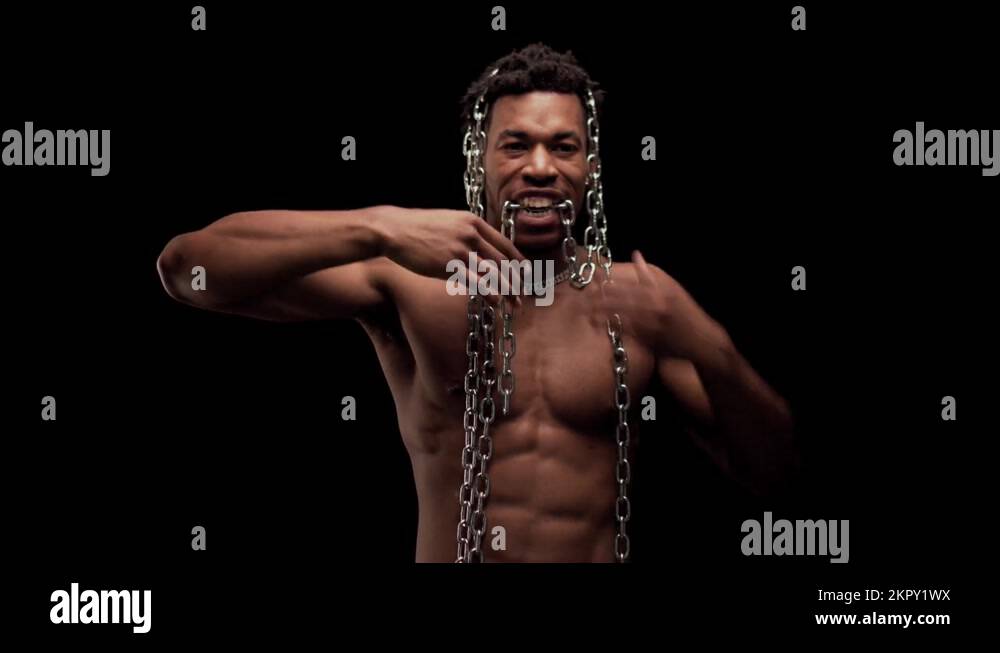 Muscular man showing muscles and biting a metal chain. African American ...