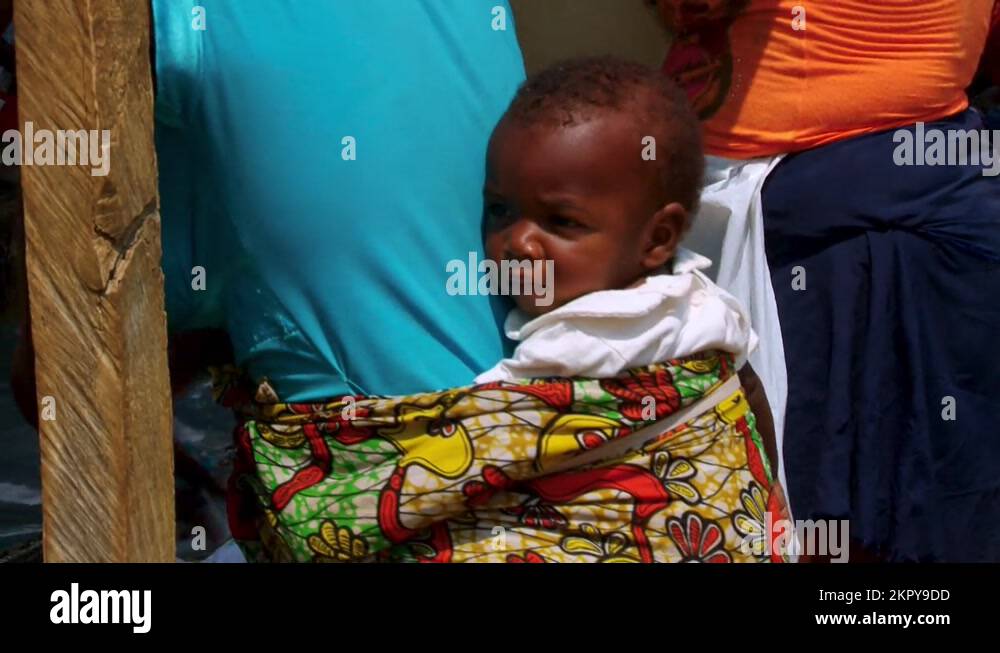Baby tied on mother's back as she does laundry on a washboard at the ...