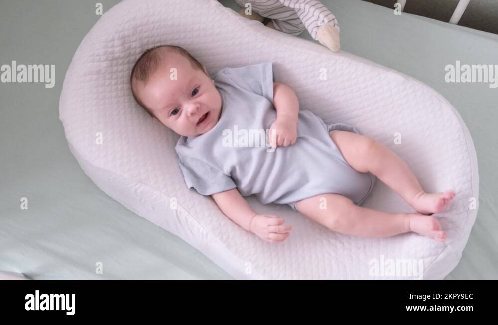 Newborn baby boy lying in nursery cocoon with blue clothes on bed in ...