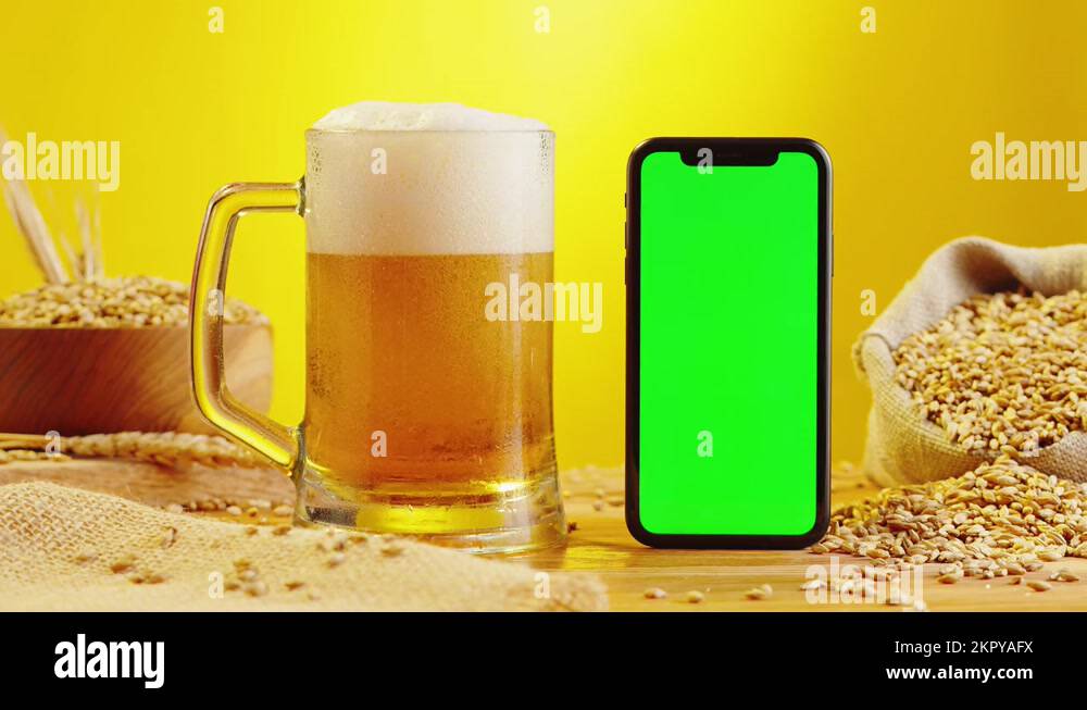 Foamy beer in glass and phone with green chroma key screen. Alcohol ...