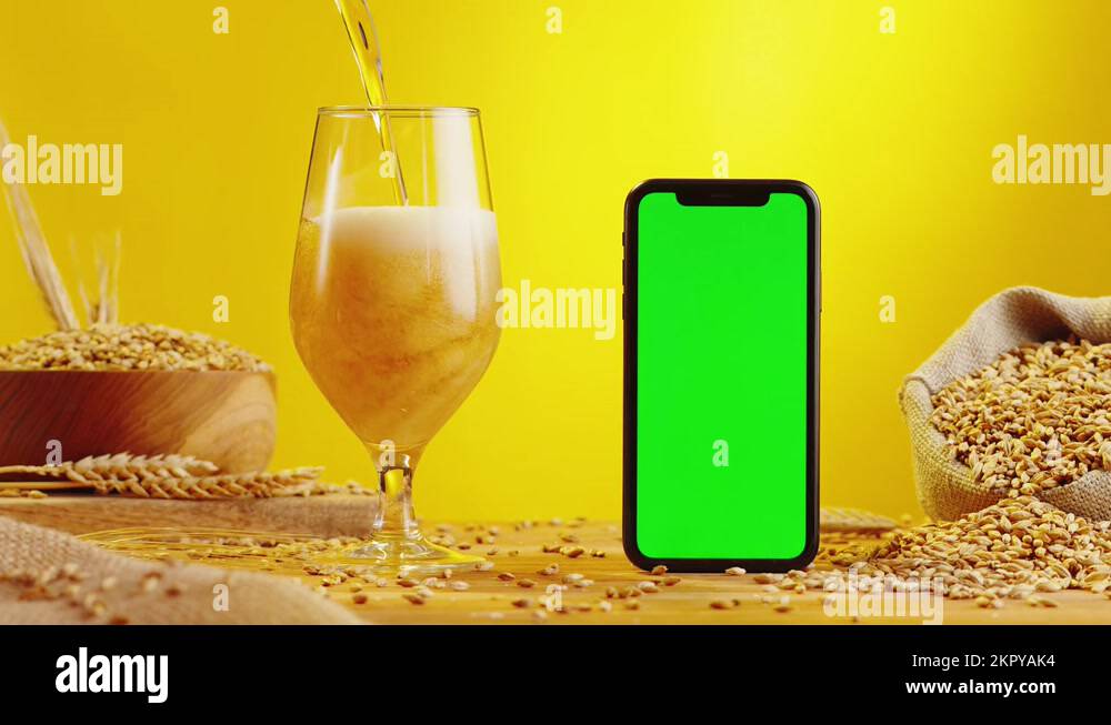 Foamy beer in glass and phone with green chroma key screen. Alcohol ...