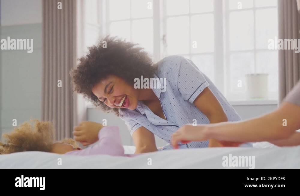 Family With Two Mums Wearing Pyjamas Playing On Bed At Home With ...