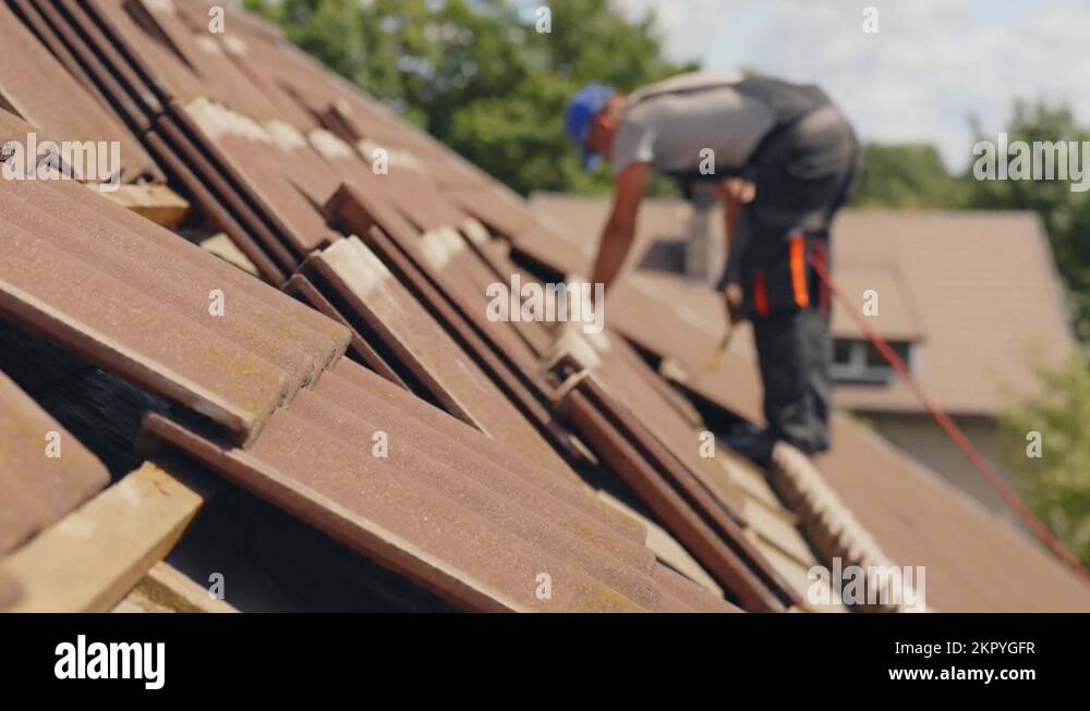 Roofer placing tiles in a house roof. Side view of construction work ...