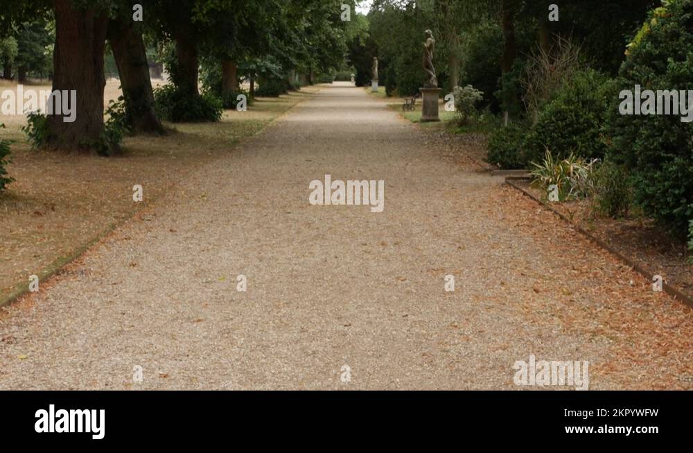 A gravel driveway in the palace mansion gardens with statues and trees ...