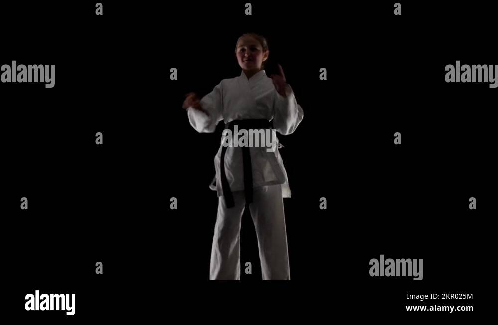 Young karate girl wearing kimono and dancing against black background ...