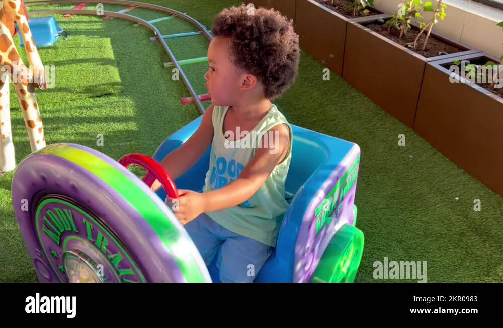 Cute and exotic two year old afro european child riding a toy train ...