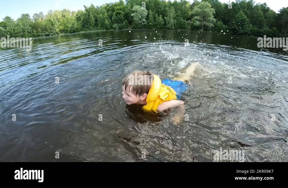 Baby boy in inflatable safety life vest floating at lake with splashing ...