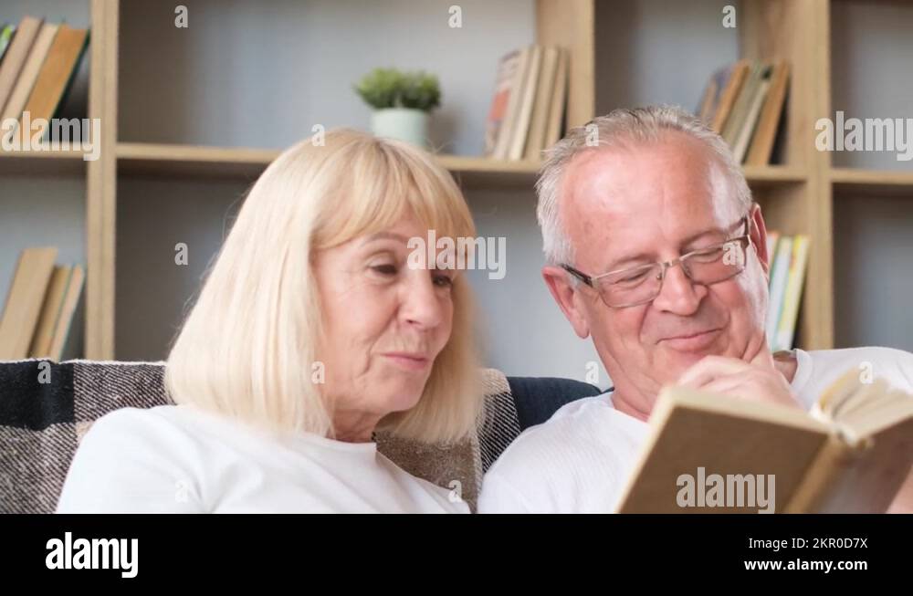 Happy Old Married Couple Reading Book Together In Home Library Stock