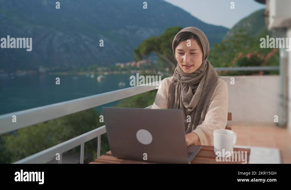 Arab young muslim woman in hijab sits balcony using laptop, middle ...