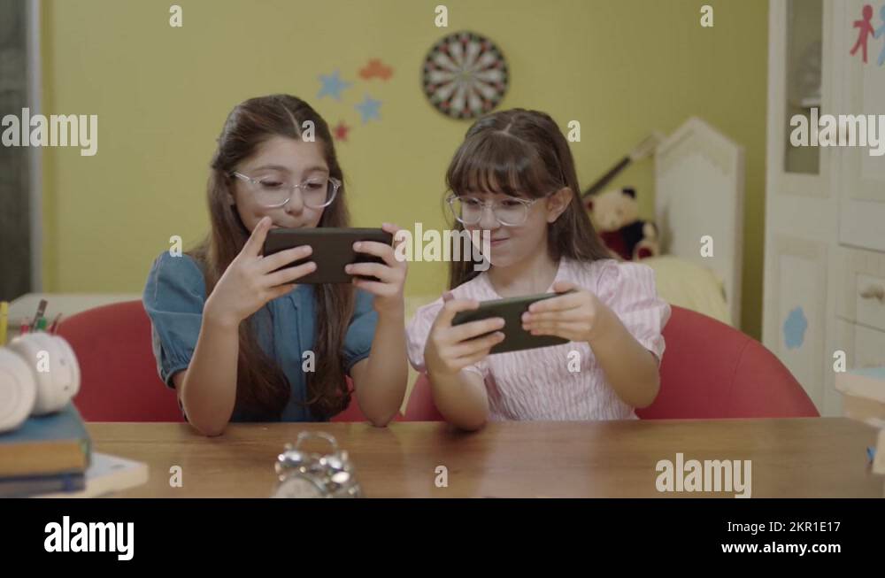Two little girl friends playing online games with smartphones at home ...