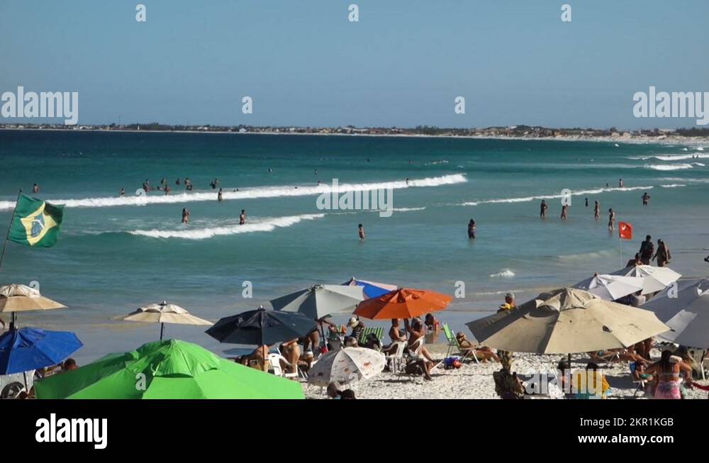 Brazilian flag hoisted at Praia do Forte beach, full of people having ...