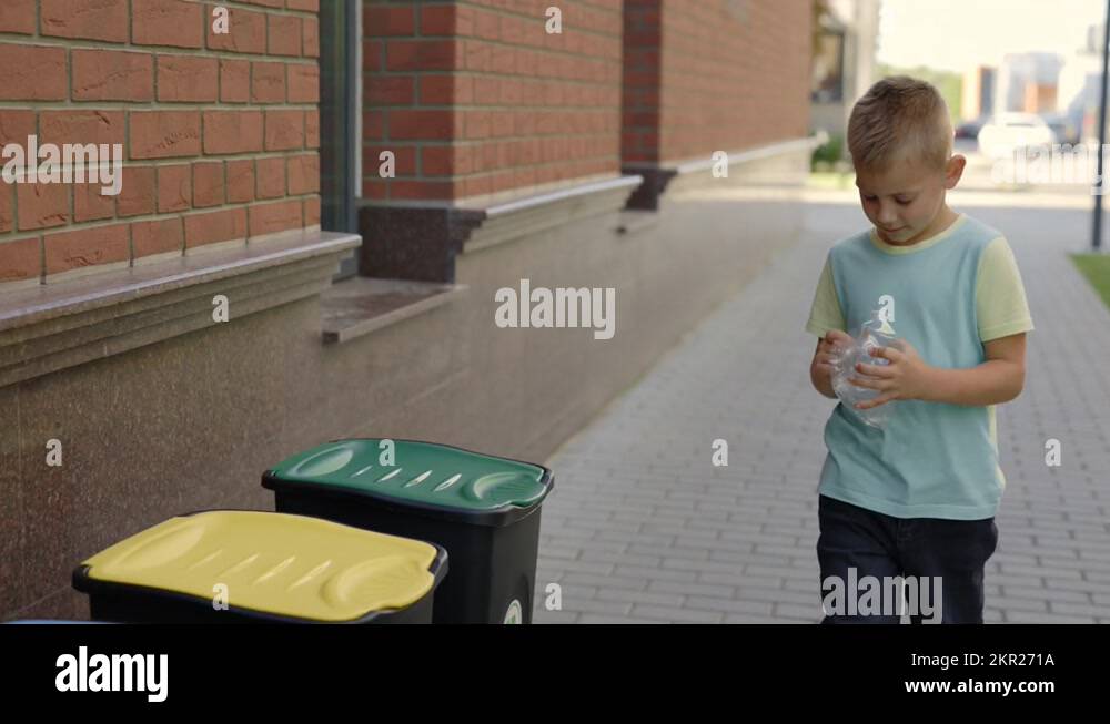 School boy is holding the plastic bottle and puts it to the correct bin ...