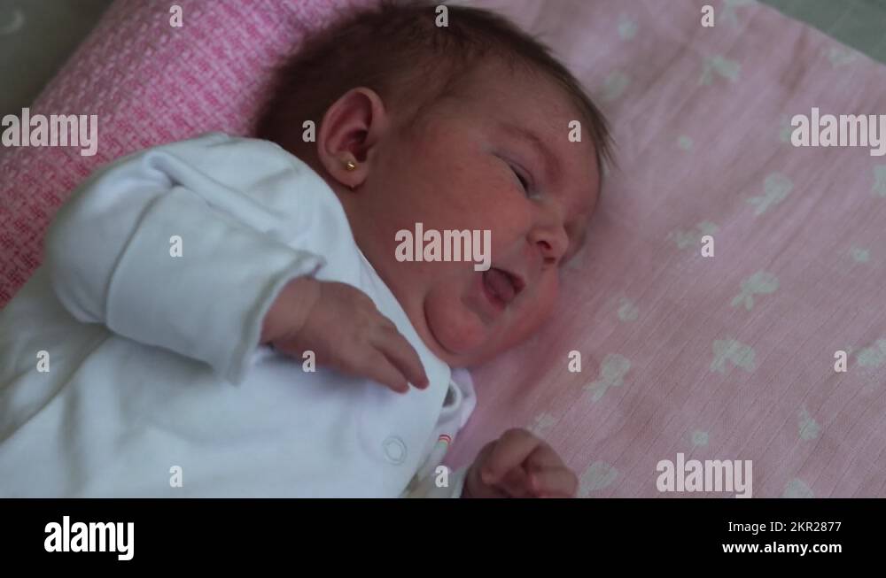 Newborn baby girl yawns, stretches and wiggles while lying on pink ...