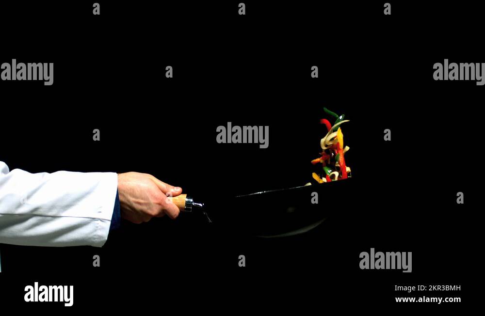Chef tossing vegetables in a wok side view on black background Stock ...
