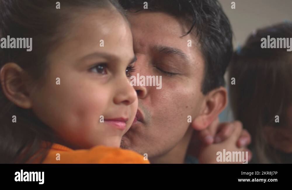 A man sits on his sofa next to two young girls who kiss and hug him ...