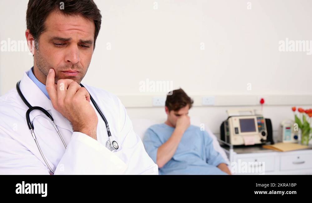 Sick man lying on hospital bed with doctor frowning at camera Stock ...
