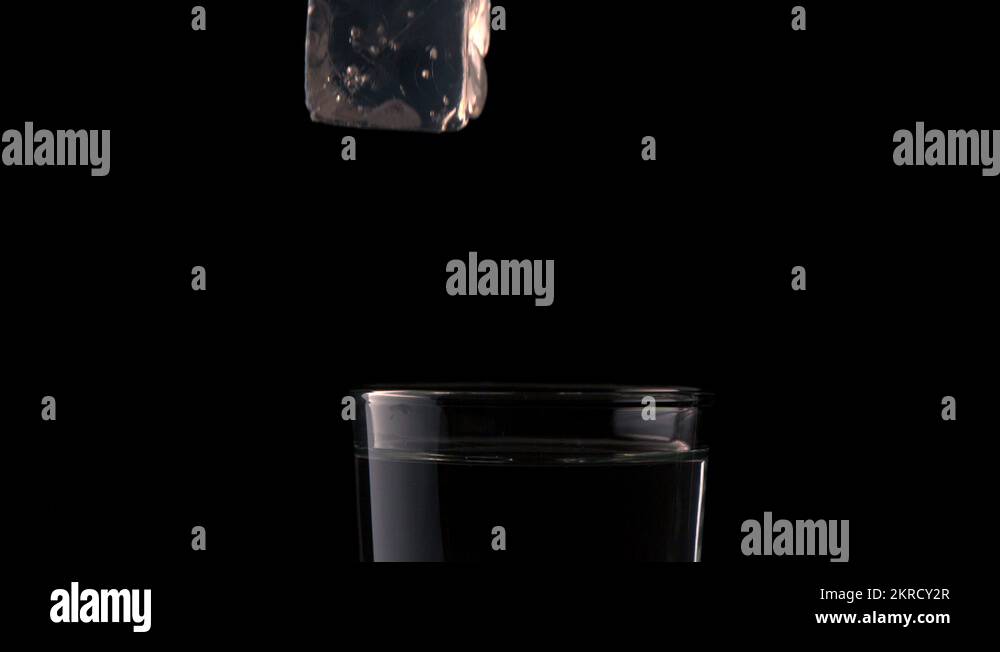 Ice cube falling into glass of water on black background Stock Video Footage - Alamy
