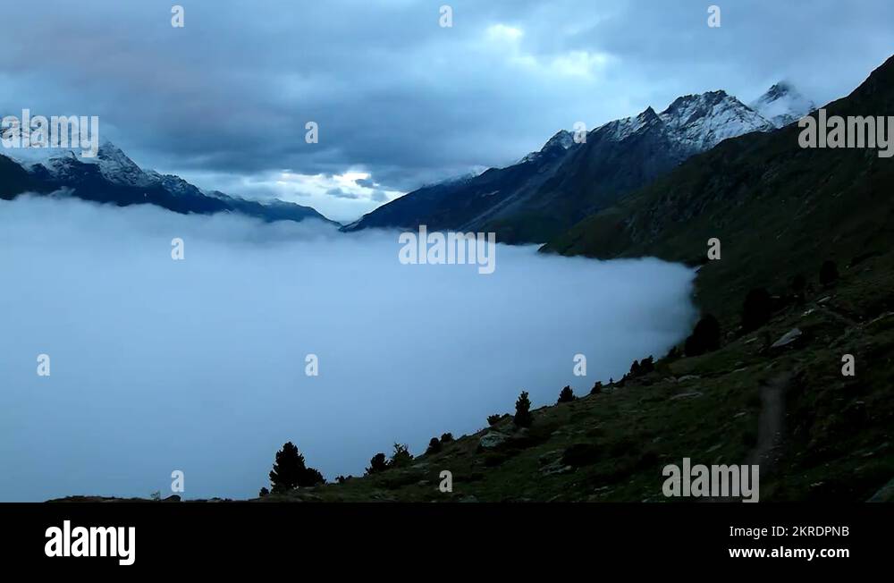 Alpine mountains sticking out from heavy mist clouds, deep valleys full ...