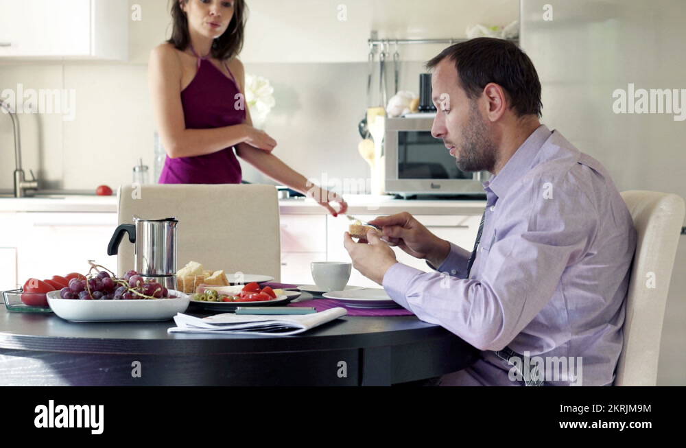 Man spreading butter on bread and talking with his wife in the kitchen ...