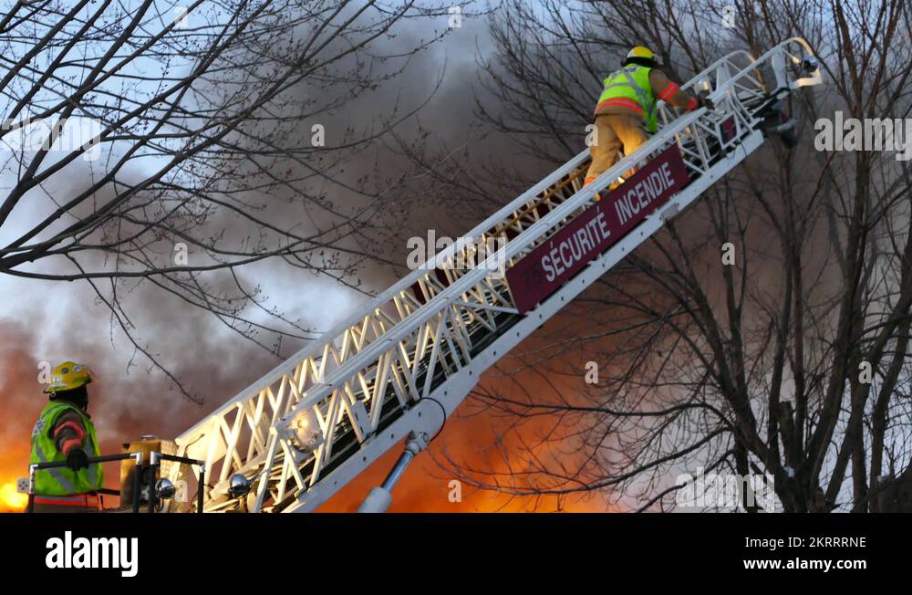 Fireman climbing up a ladder with house fire and heavy flames ...