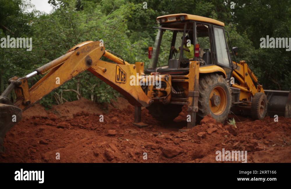 JCB Bulldozer tractor digging soil with Indian worker carrying ...