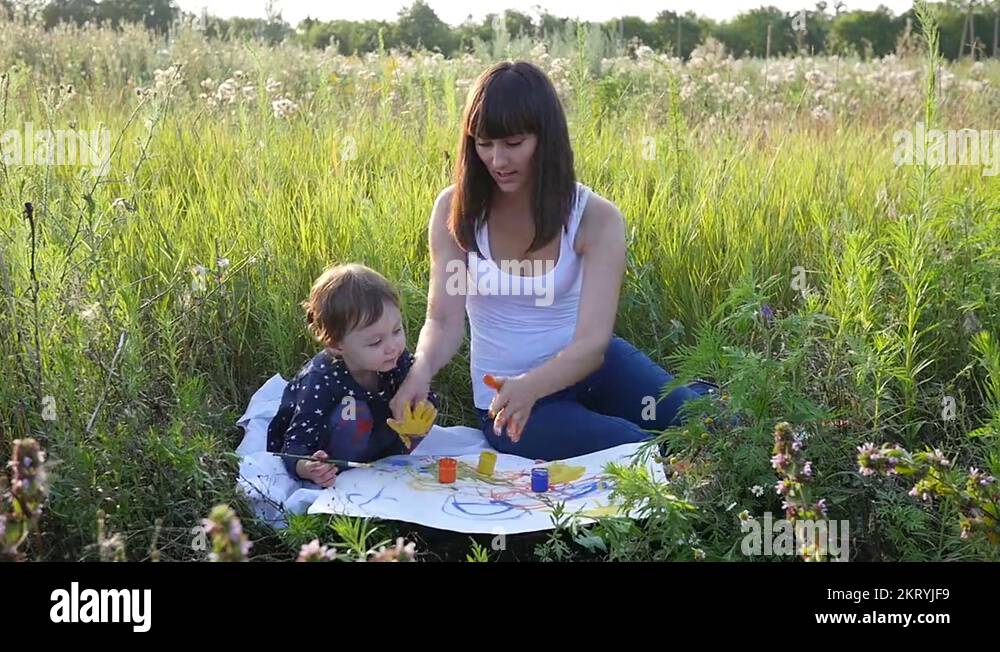 Mom and little daughter fun paint drawing handprints on nature sunset ...