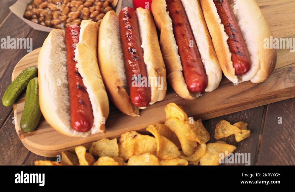 Grilled hot dogs on a white hot dog buns with chips and baked beans on ...