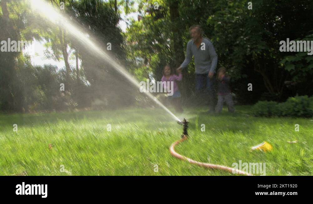LS OF A FATHER AND HIS DAUGHTERS RUNNING THROUGH A SPRINKLER Stock ...