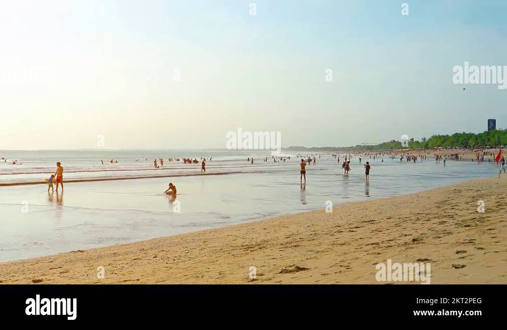 Tourists crowd a tropical beach to enjoy the sun and surf in Kuta, Bali ...