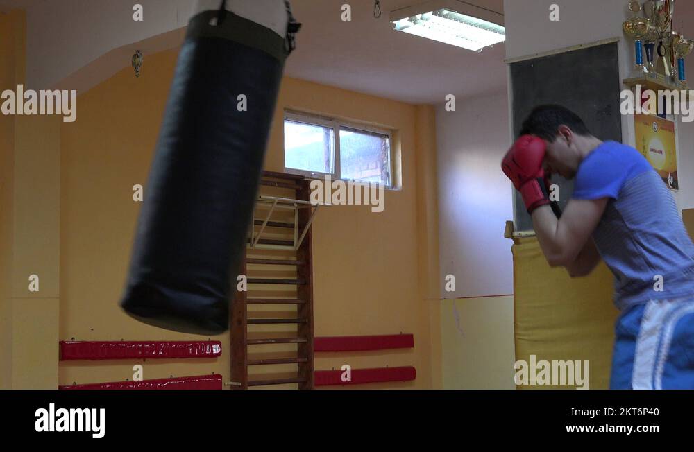 Young boxer aggression, powerful punch at punching bag, reg gloves ...