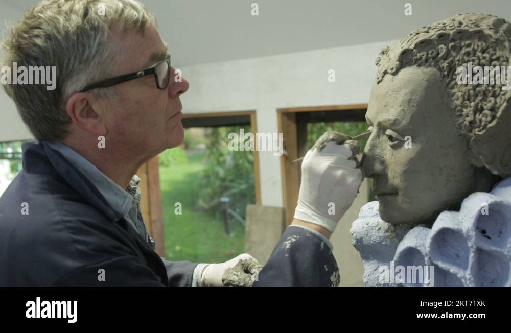 A male sculptor using a tool to model a clay statue ready to be cast in ...