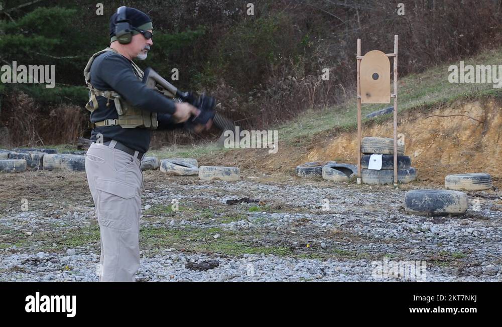 Man in tactical gear loading and firing an AR-15 rifle at a target ...