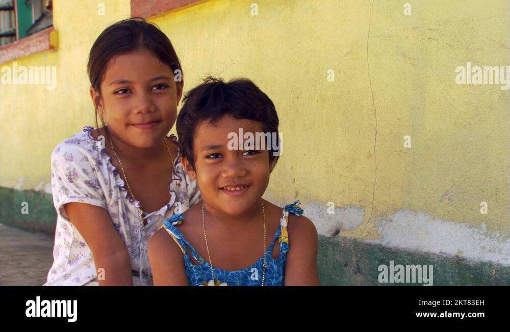 Smiling Samoan sisters sitting for portrait in front of yellow stucco ...