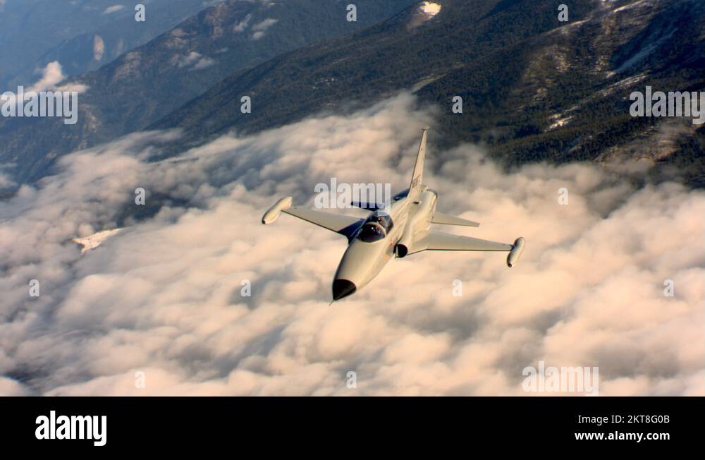 Northrop F-5A fighter jet flying over clouds above rugged mountain ...