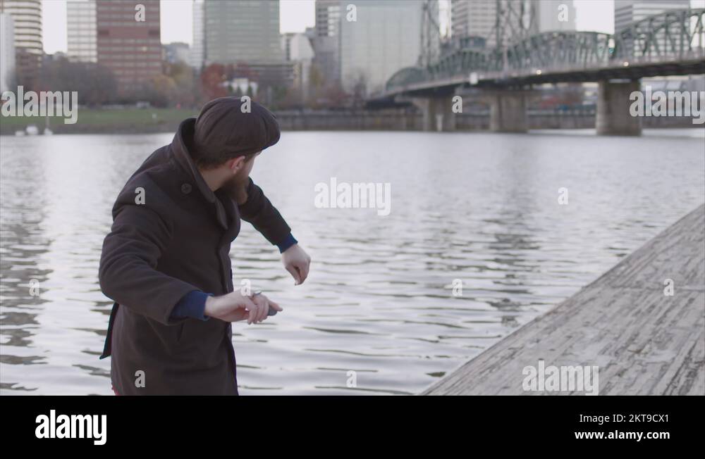 Well-dressed man skipping rocks on a river off of a dock in the city by ...