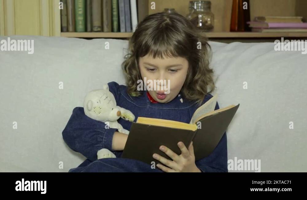 Little girl reading a book aloud teddy bear in the living room on the ...