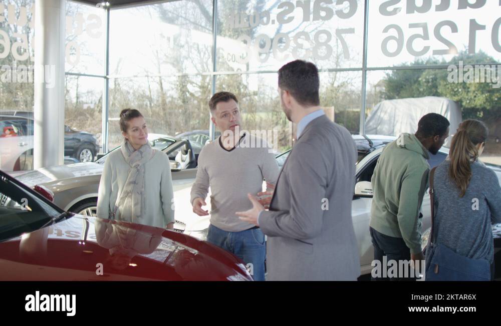 4K Salesman in car dealership with couple, showing them the engine of ...