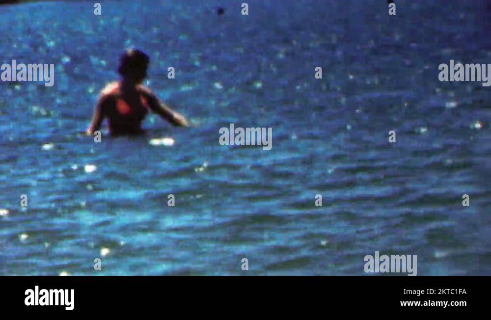 1961: Bikini clad woman wading in deep glistening blue ocean water ...