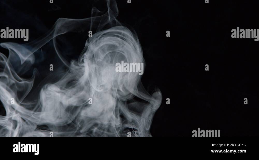 Billows of white turbulent smoke rise through frame against black ...