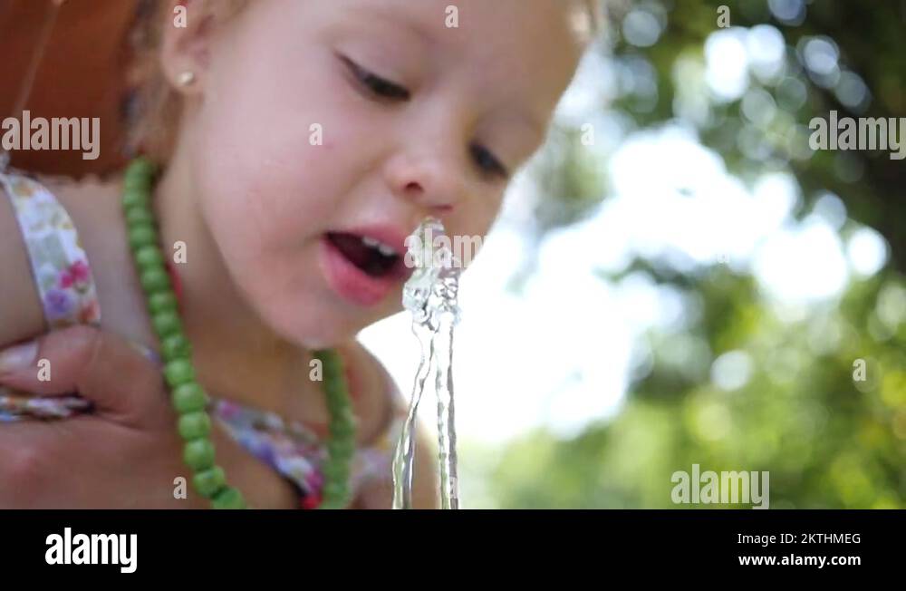 Little child girl funny catch water jet with mouth drink from drinking ...