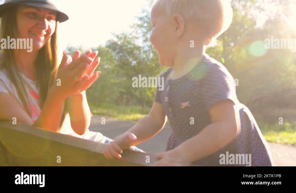 Mom with a one year old baby girl playing pat-a-cake on a park bench ...