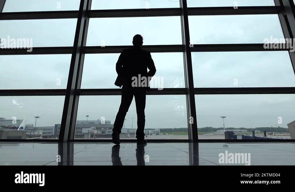 Man come and stand at full height, gaze out airport terminal window ...