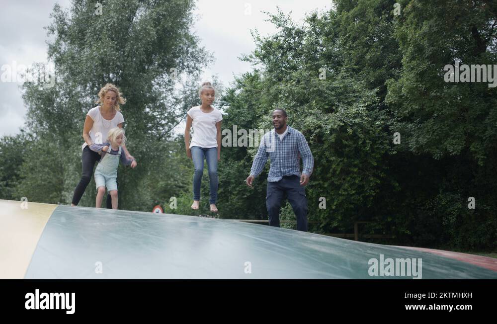 4K Happy mixed race family having fun, jumping on inflatable at ...